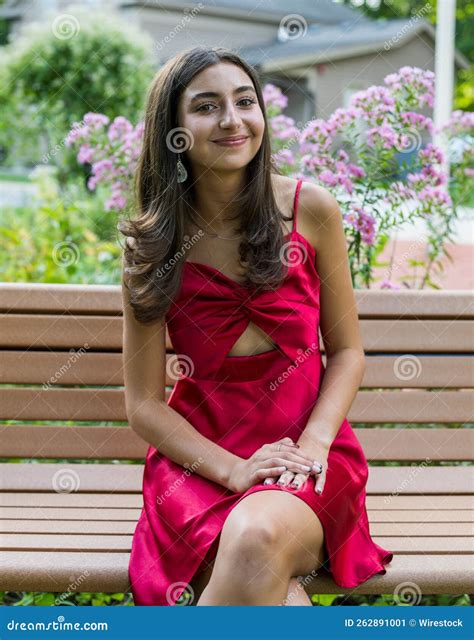 Teenage Girl Sitting On Park Bench With Red Dress Smiling Without