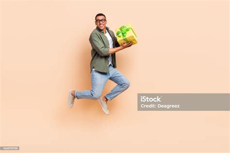 멋진 쾌활한 남자의 전체 길이 사진 입은 카키색 셔츠 점프 높은 들고 선물 상자 격리 된 베이지 색 배경 공휴일에 대한 스톡 사진 및 기타 이미지 Istock
