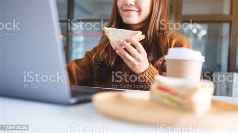 랩톱 컴퓨터에서 작업하는 동안 통밀 샌드위치를 들고 먹는 여성 노트북 사용하기에 대한 스톡 사진 및 기타 이미지 노트북