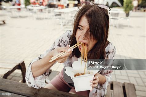 테이크아웃 종이 상자에 국수를 먹는 배고픈 보헤미안 여자 음식 배달 아시아 거리 음식 축제입니다 대나무 젓가락으로 판지 상자에서 야채와 함께 냄비를 먹는 세련 된 소식통