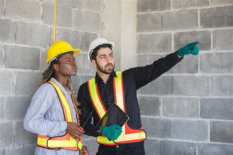 남자 백인 엔지니어 감독관 그리고 미국인 아프리카 일반 직원들이 마을 부동산 건설 현장에서 함께 일하고 있습니다 건설 감독 노동자 건축가 20 24세에 대한 스톡 사진 및