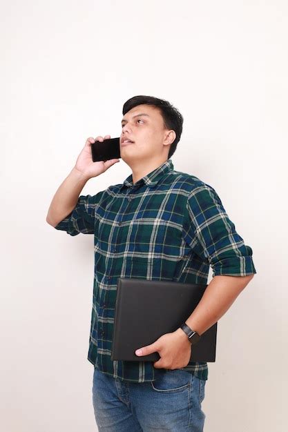 Premium Photo Young Asian Man Holding A Laptop While Talking On The Phone