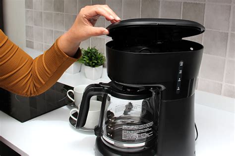 여성의 손은 물과 갓 빻은 커피로 아침 식사를 위해 부엌의 커피 메이커에서 맛있고 향기로운 커피를 준비합니다 가정 생활에 대한