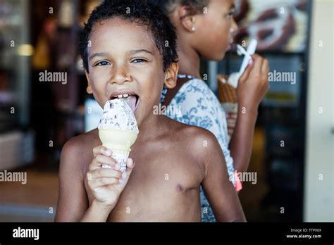 Portrait Of Shirtless Brother Licking Ice Cream While Standing By
