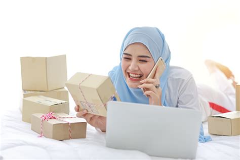 매력적인 표정을 가진 잠옷을 입은 아름답고 젊은 아시아 무슬림 여성은 컴퓨터와 온라인 패키지 상자 배달로 침대에 누워 있다 스타트업 중소기업 프리랜서 소녀 휴대 전화 작업