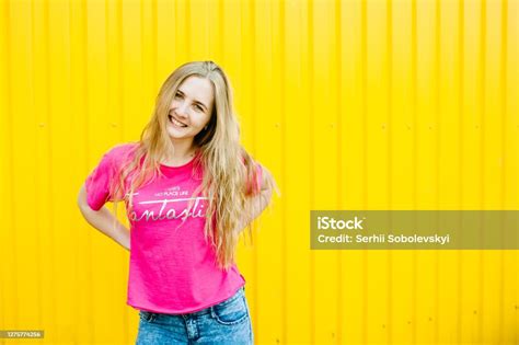 핑크 셔츠와 청바지에 긴 금발 머리를 가진 아름다운 운동 젊은 여자 노란색 배경에 차고의 벽에 포즈와 미소 벨트에 손을 텍스트에 대 한 배치 클로즈업 미소 25 29세에