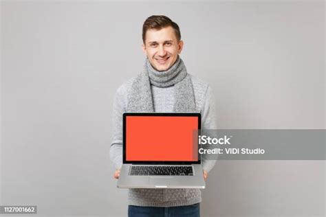 회색 스웨터 스카프 빈 빈 화면 회색 배경에 고립 된 노트북 Pc 컴퓨터를 들고 웃는 젊은 남자가 있다 건강 온라인 치료 컨설팅 추운 계절 개념 복사 공간을 비웃는 다