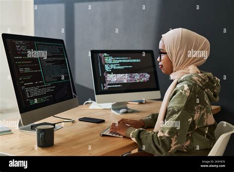 Side View Of Young Muslim Female Programmer Looking Through Coded Information On Computer Screen