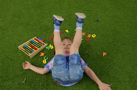 유치원에 다니는 한 어린이가 읽고 숫자를 세는 법을 배웁니다 미취학 아동이 글자와 나무 주판 주위에 푸른 잔디밭에 누워 있습니다 영어 배우기 4 5세에 대한 스톡 사진 및