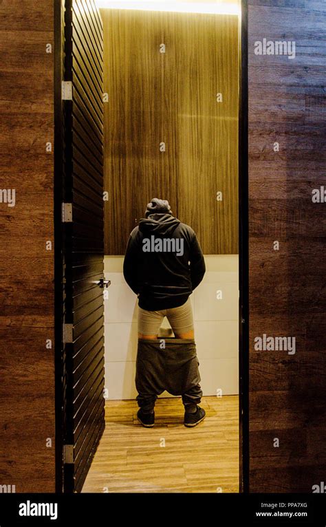 Man Standing Peeing A Urinal With Pants Down In The Bathroom Or