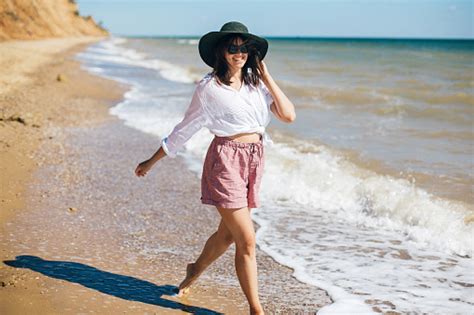 여름 방학 열대 섬과 푸른 하늘에서 화창한 따뜻한 날에 바다 파도를 걷는 행복한 젊은 보헤미안 여성 텍스트의 공백입니다 해변에서 휴식과 미소 모자에 세련된 힙스터 소녀