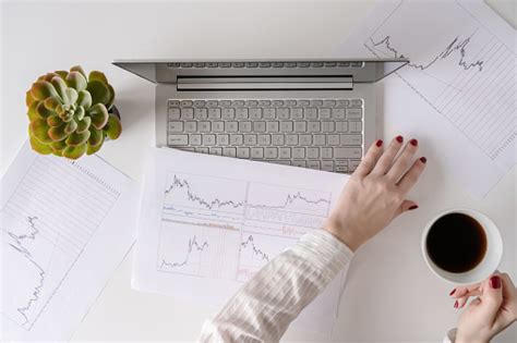 커피 한 잔과 함께 사무실 테이블에 앉아 종이에 인쇄 된 그래픽과 차트와 노트북에서 작업하는 동안 여성 프리랜서 작업 및 노트북의 키보드에 입력 플랫 레이 거래자에 대한