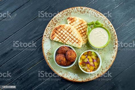 피타 빵을 곁들인 팔라펠은 어둡고 우디한 배경을 배경으로 녹색 접시에 흰색 소스와 피클을 곁들인 식욕을 돋우는 동양 요리입니다 채식 음식 음식에 대한 스톡 사진 및 기타