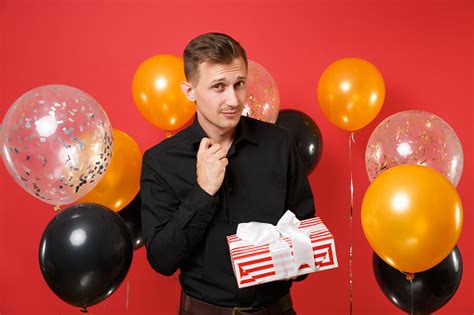 클래식 셔츠에 잘생긴 젊은 남자 선물 빨간 배경 공기 풍선에 빨간색 상자를 들고 칼라 직선 성 발렌타인의 날 해피 뉴가 어 생일 이랑 휴일 파티 개념 남자에 대한 스톡 사진