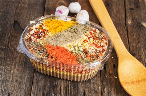 어두운 나무 배경에 나무 숟가락 옆에 플라스틱 용기에 혼합 건조 인도 다채로운 향신료의 상단보기 요리 재료 후추 칠리 카레 사프란과 아시아 요리의 개념 가루로 빻은에 대한