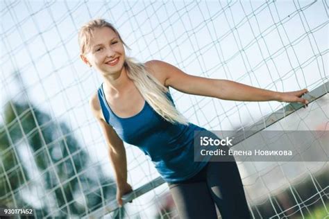 블루 셔츠와 레 깅 스에 소녀는 일몰에 경기장에서 축구 목표 근처 카메라와 미소 서 보인다 여자 완벽 한 그림을 그리고 좋은