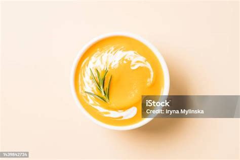 밝은 배경 위에 헤비 크림과 로즈마리로 장식된 흰색 그릇에 담긴 두꺼운 버터넛 스쿼시 비스크 호박과 당근 크림 수프 한 그릇