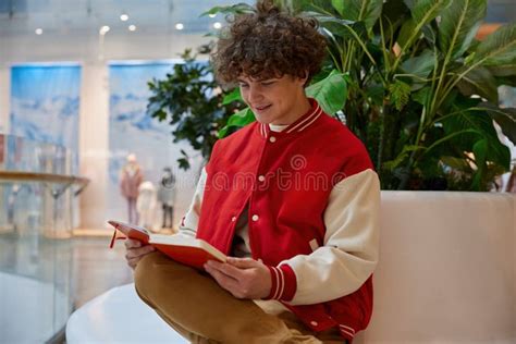 Handsome Teenage Boy Reading Book While Rest In Shopping Mall Stock
