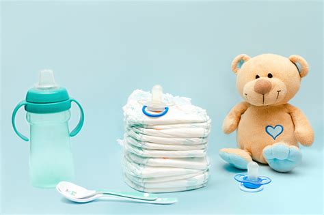 귀여운 테디 베어 장난감 병 우유 젖꼭지 테이블에 숟가락이 있는 기저귀 더미 아기 신생아 소년 소녀를 위해 설정된 베이비 샤워 선물 파란색 배경에 선물 의료 의료 위생 개념