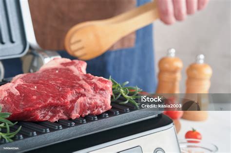 전기 그릴에 생 프라임 스테이크 로즈마리 방울 토마토 후추를 곁들인 현대적인 전기 그릴에 스테이크 립아이를 들고 있는 셰프 남성