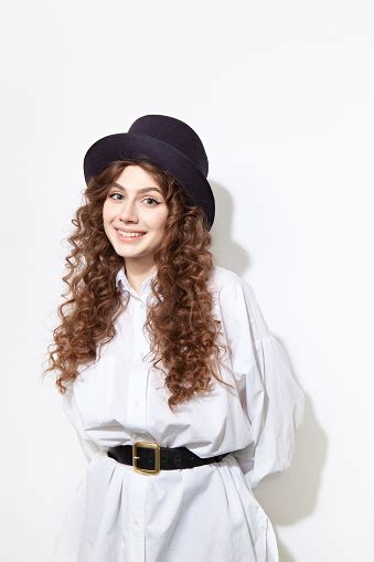 흰색 셔츠와 흰색 배경에 모자를 쓰고 곱슬 갈색 머리를 가진 20 세 여성의 스튜디오 초상화 20 24세에 대한 스톡 사진 및 기타 이미지 Istock