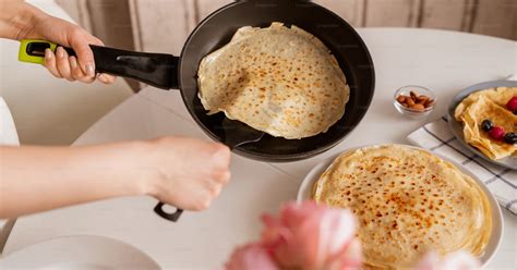 뜨거운 식욕을 돋우는 팬케이크를 접시에 다른 크레이프 위에 올려 놓는 동안 식탁 위에 프라이팬을 들고 있는 젊은 여성의 손 사진