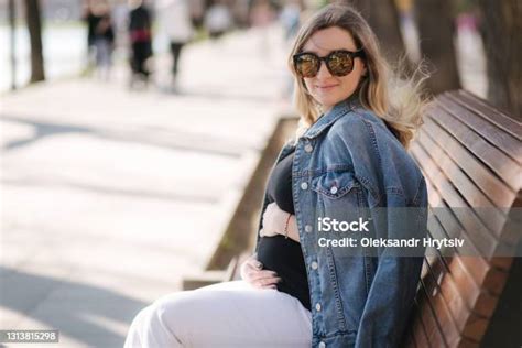 행복한 임산부는 배에 손을 얹고 카메라를 보고 있습니다 공원에서 벤치에 앉아 있는 여성 미래의 어머니는 신선한 공기를 호흡 건강한 생활방식에 대한 스톡 사진 및 기타 이미지