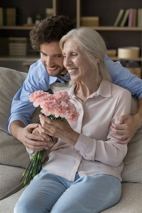 Older Woman Holding Flowers Enjoy Cuddles Of Grownup Son Stock Image