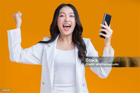 깜짝 얼굴 표정 아시아 비즈니스 여성 여성 손 제스처가 스마트 폰 화면 디스플레이에서 성공적인 진행 결과와 함께 종료되어 밝은 노란색으로 격리 된 손을 들어 나갔습니다 25