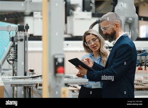 Female Engineer And Male Production Manager Standing In Modern Industrial Factory Talking About