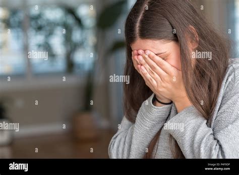 Young beautiful woman at home with sad expression covering face with hands while crying ...