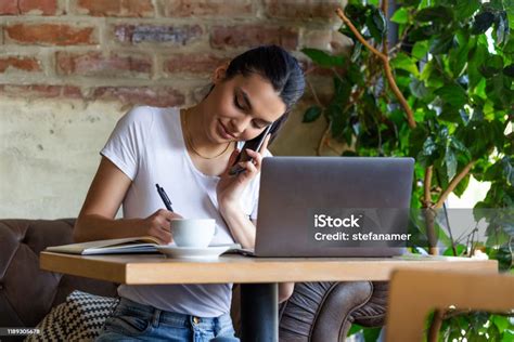 커피숍에 앉아 커피를 마시고 모바일 스마트폰을 사용하는 젊은 여성 테이블에 노트북입니다 소녀 인터넷 검색 채팅 블로그 그녀의 전화에 이야기하고 메모를 복용 하는 여성 20