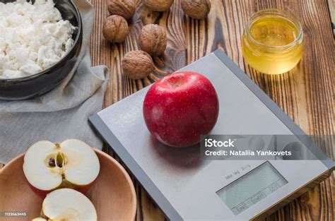 빨간 사과는 나무 테이블에 금속 눈금에 놓여 있으며 옆에는 코 티 지 치즈 자른 사과 견과류 거짓말과 꿀 항아리가 있는 접시가 있습니다 건강한 식생활에 대한 스톡 사진 및