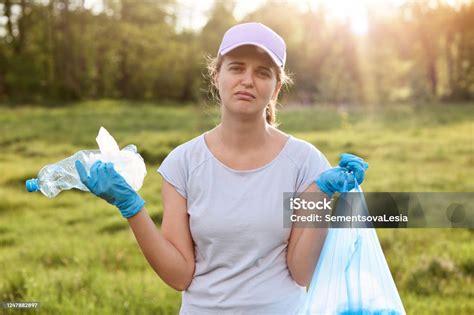 현장에서 쓰레기를 줍고 아무렇지 않게 입고 쓰레기 봉투를 들고 피곤하고 화가 난 표정으로 카메라를 바라보며 공원 전체를 청소하고 환경 문제를 해결합니다 가방에 대한 스톡