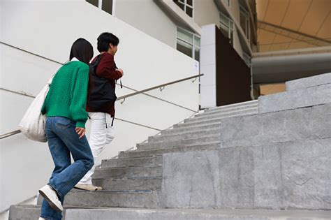 두 명의 학생들이 학교로 돌아가 손을 잡고 대학 위층으로 올라가고 여자 친구는 수업을 위해 수업에 달려갑니다 큰 배낭을 메고 손을 잡고 수업에 간다 2명에 대한 스톡 사진