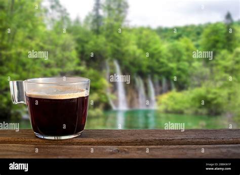 Glass Cup Of Black Coffee With Waterfall In The Forest Blur Background