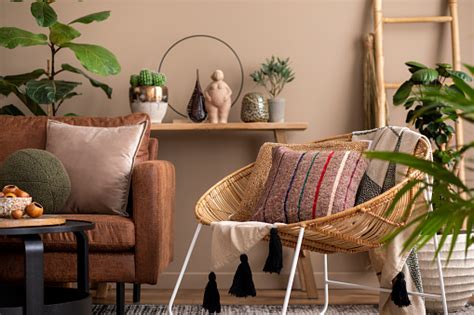 갈색 소파 꼰 안락의자 무늬 베개 둥근 커피 테이블 세련된 조각품 화분 식물 및 개인 액세서리가 있는 거실 인테리어의 인테리어 디자인 가정 장식 템플렛 0명에 대한 스톡