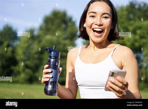 Une jeune femme asiatique excitée s entraîne et boit de l eau suit l application sportive sur