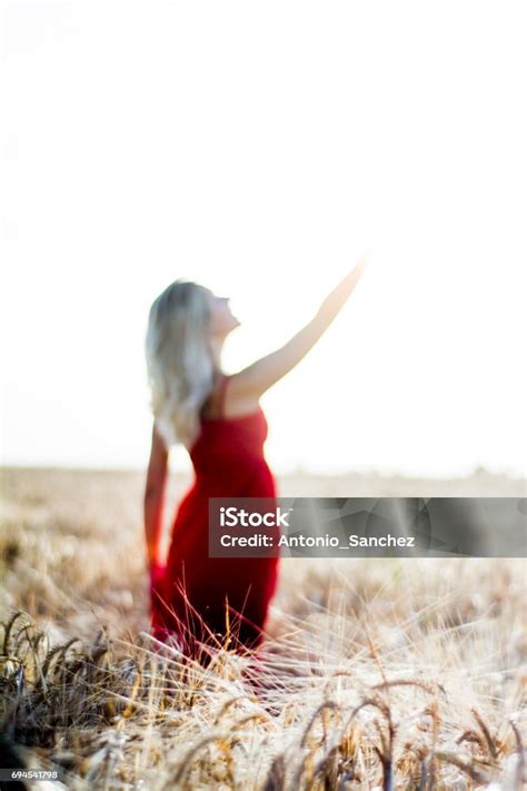 Backlit Portrait Of Beautiful Blond Woman In A Red Dress On A Wheat