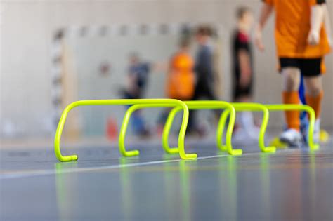 노란색 장애물이있는 실내 스포츠 훈련 장애물을 뛰어 넘고 뛰어 다니는 어린 소년 겨울철에 실내 스포츠 수업을하는 학교 아이들