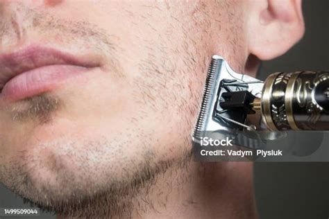 남자는 전기 금속 면도기 또는 건식 면도기로 수염을 자르고 있습니다 절단을위한 트리머 남자 얼굴에 짧고 희소 한 수염 모발 성장