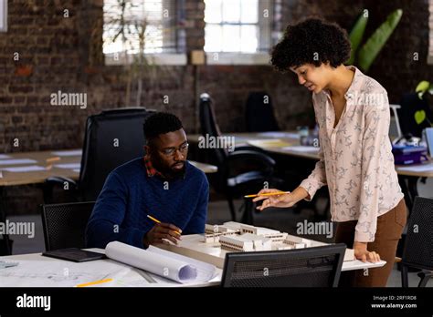 Diverse Male And Female Architects Looking At Building Model And Discussing Project At Office