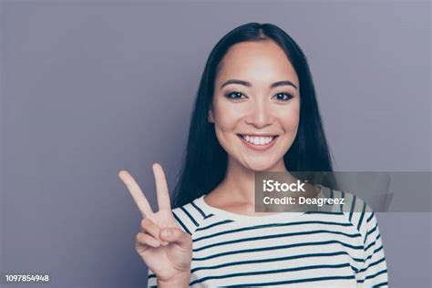 그녀가 그녀의 지주 손 인사에서 Vsign 그림 형태로 안녕 말 입고 흰색 스웨터 회색 배경에 고립 꽤 놀라운 갈색 머리의 초상화를 닫습니다 브이에 대한 스톡 사진 및 기타