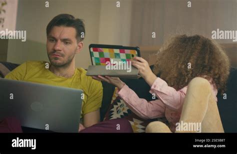 Young Dad Sitting On Sofa With Laptop An Eight Year Old Girl Shows Him