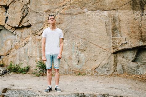 남자는 큰 돌에 큰 바위 벽의 배경에 서 Grimace를 만든다 전체 길이 카메라를 보고 있습니다 닫습니다 텍스트와 디자인을 위한 장소 남자는 자연에 산의 절벽에 포즈