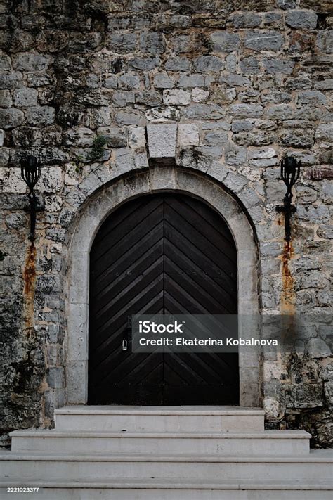 갈매기 모양이 있는 검은색 나무 문 아치형 돌 입구 안에 있습니다 질감 있는 돌벽과 연철 랜턴은 역사적이고 우아한 느낌을 더하며 자물쇠는 문을 고정합니다 0명에 대한 스톡