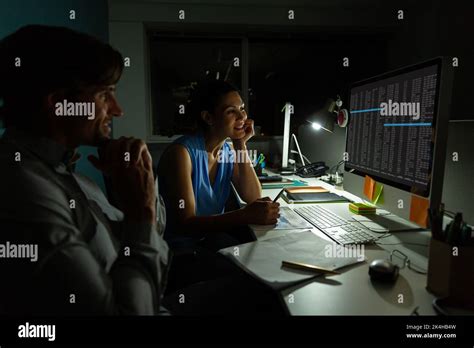 Two Diverse Male And Female Colleagues Sitting At Desk Using Computer With Coding On Screen