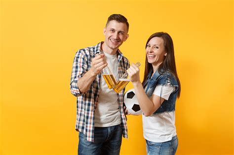 젊은 행복 한 명랑 커플 지지 여자 사람 축구 팬 들 응원 지원 팀 맥주 병 노란 배경에 고립 된 축구공을 들고 스포츠 가족 레저 사람들의 라이프 스타일 개념
