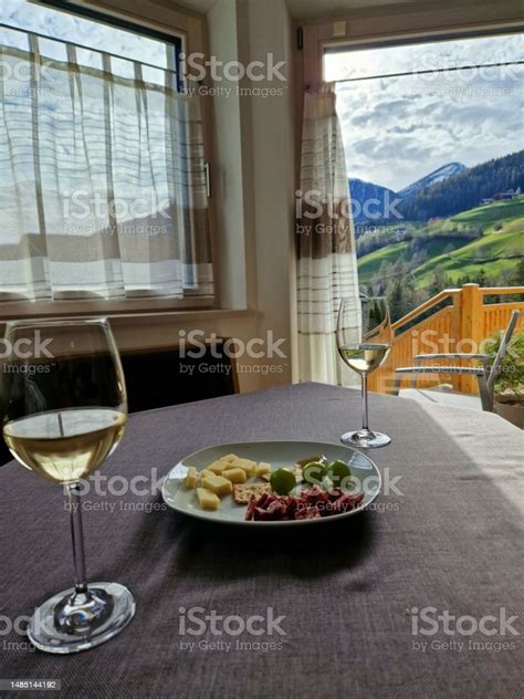 화이트 와인 두 잔과 현지 치즈와 샤퀴테리 고기 소시지 한 접시가 있는 소박한 분위기의 테이블 멀리서 바라보는 산맥과 태양의 전망 사진 이미지에 대한 스톡 사진 및 기타
