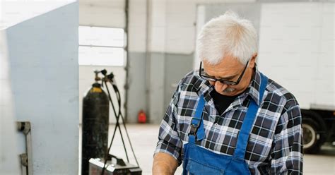 렌치를 사용하여 자동차 엔진의 부품을 고정하는 동안 작업장에 서 있는 작업복과 셔츠를 입은 수석 전문 기술자 사진 Unsplash의 산업 이미지
